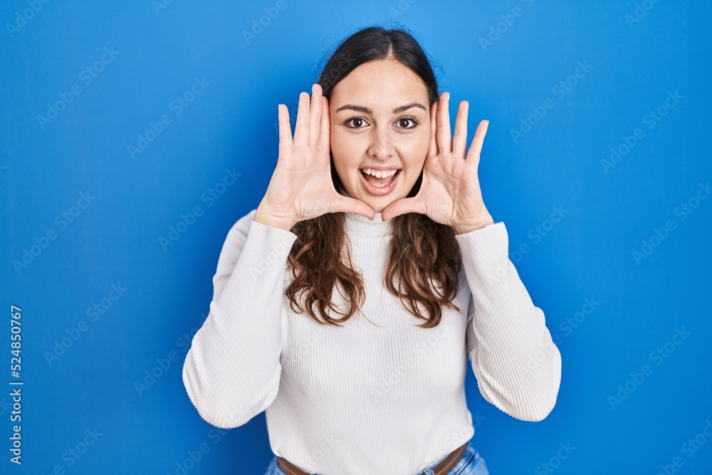 Young hispanic woman standing over blue background smiling cheerful ...
