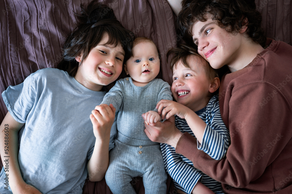 Portrait of three brothers lying on bed with their baby sibling ...