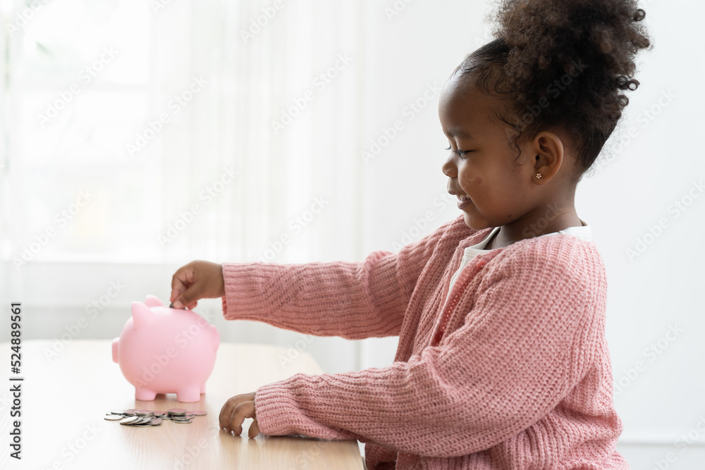 Happy African American small girl kid putting money into the piggybank ...