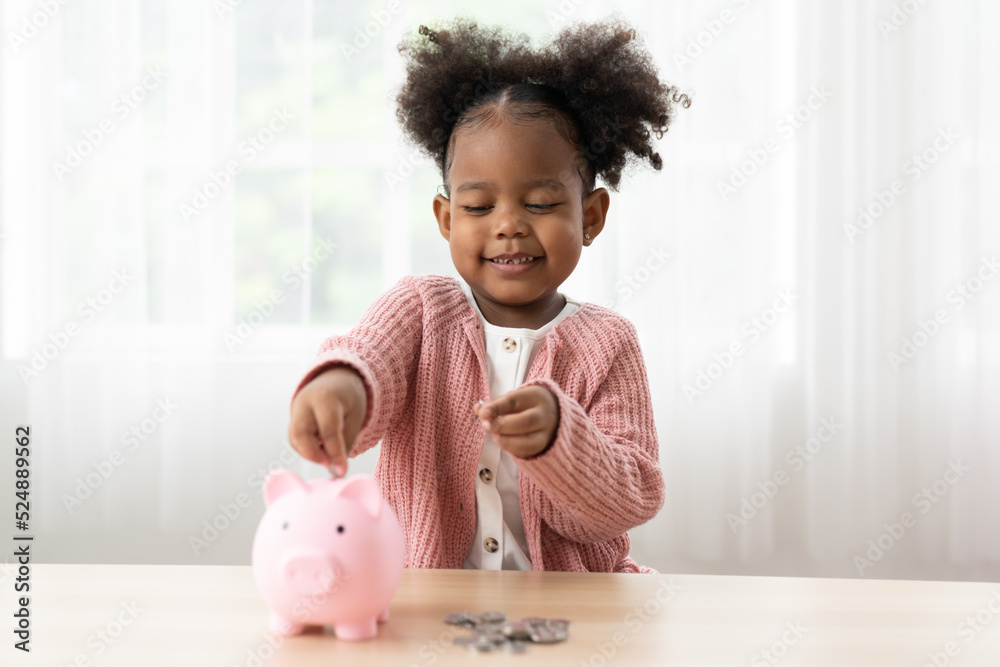 Happy African American small girl kid putting money into the piggybank ...