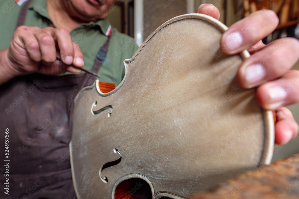 luthier carving the shape of the outside of the front of a violin with ...