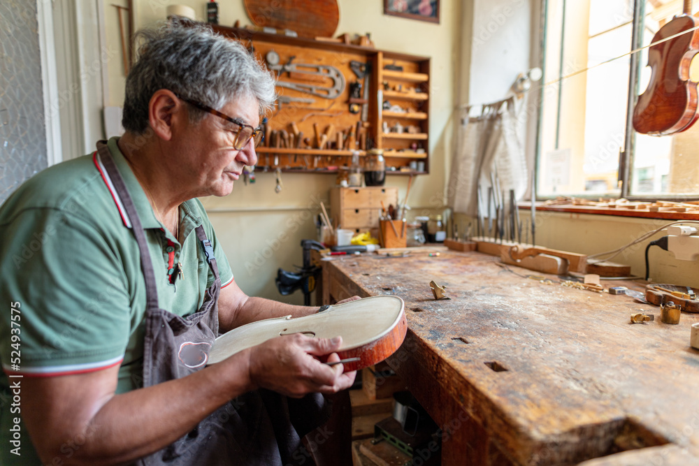 luthier carving the shape of the outside of the front of a violin with ...