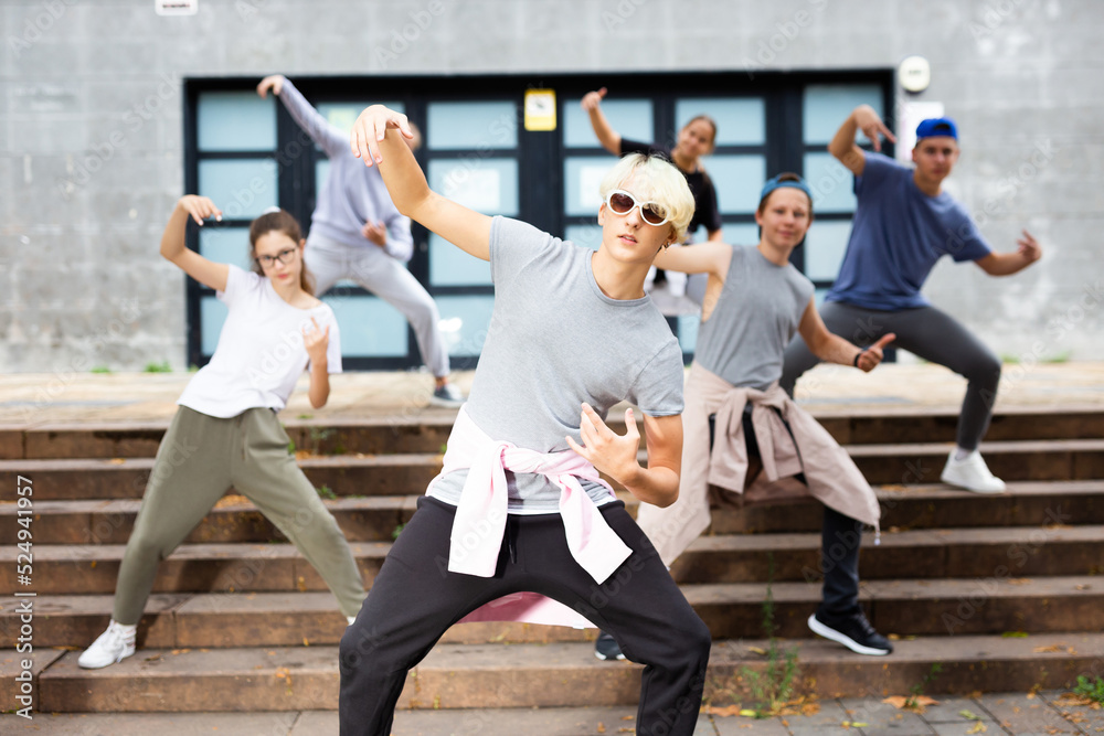 Positive teen boy dancing modern street dance outdoors with teenagers ...