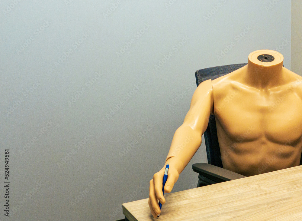 Headless Male Torso ,mannequin, sitting on a chair at a desk in a bland ...