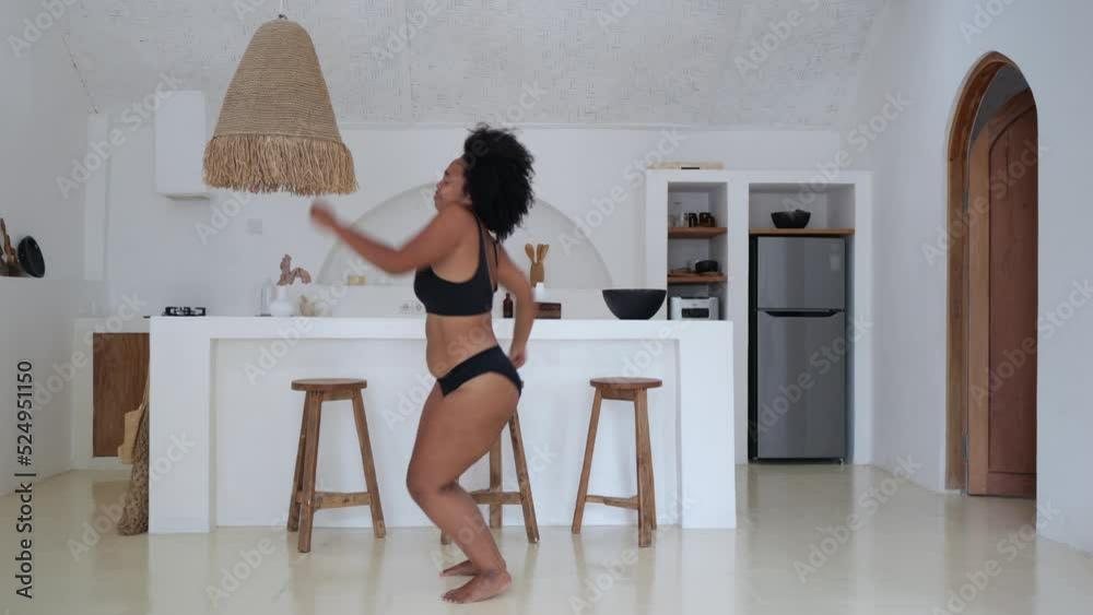 African American model plus size dancing at home in the kitchen in black lingerie. The woman ...