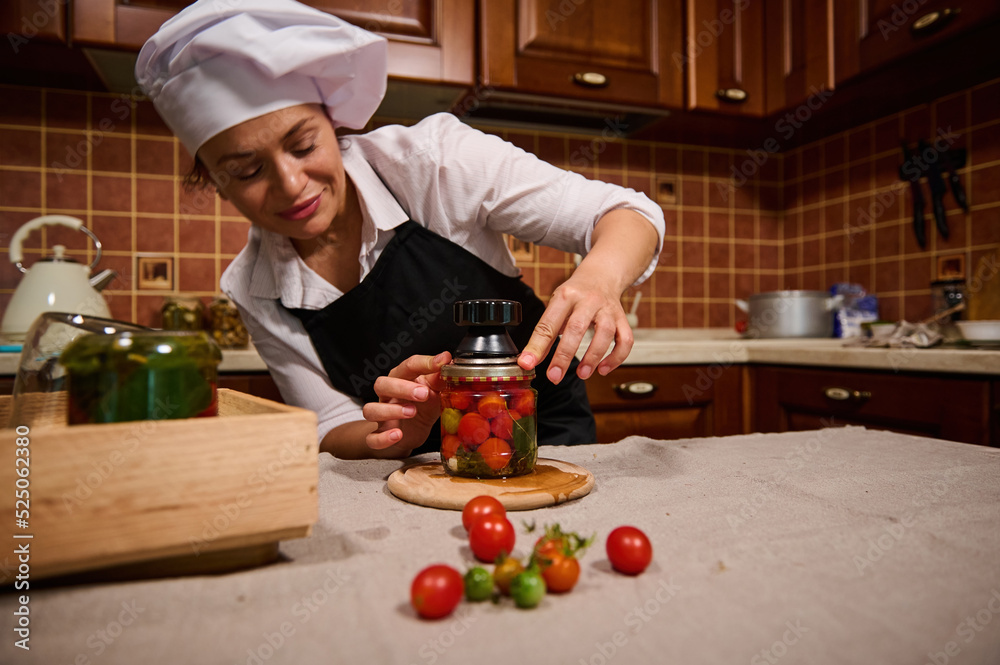 Beautiful Hispanic housewife in white chef's cap and black apron, using ...