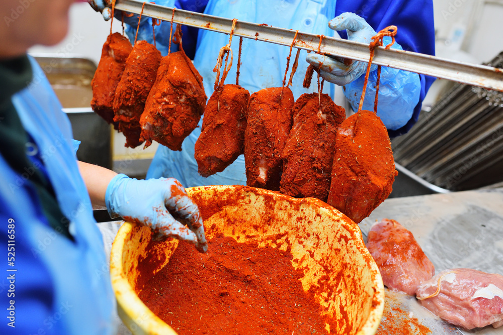 Meatpacking staff seasoning cuts of fresh pork and hanging on hooks on ...