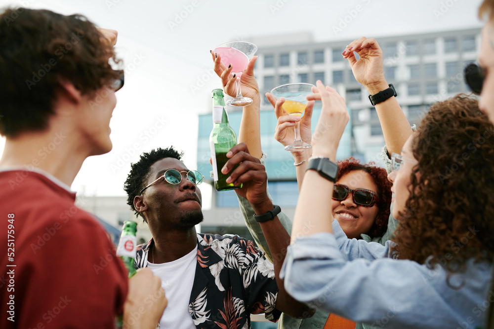 Group of cheerful friends raising hands with beer and cocktails while ...