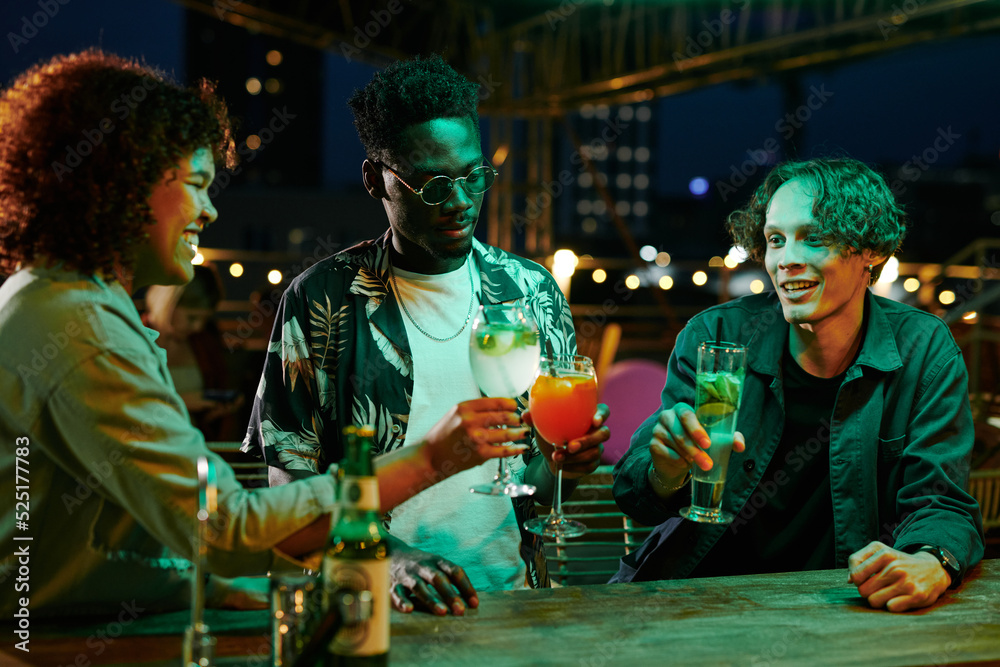 Three young multicultural friends in casualwear toasting with cocktails ...