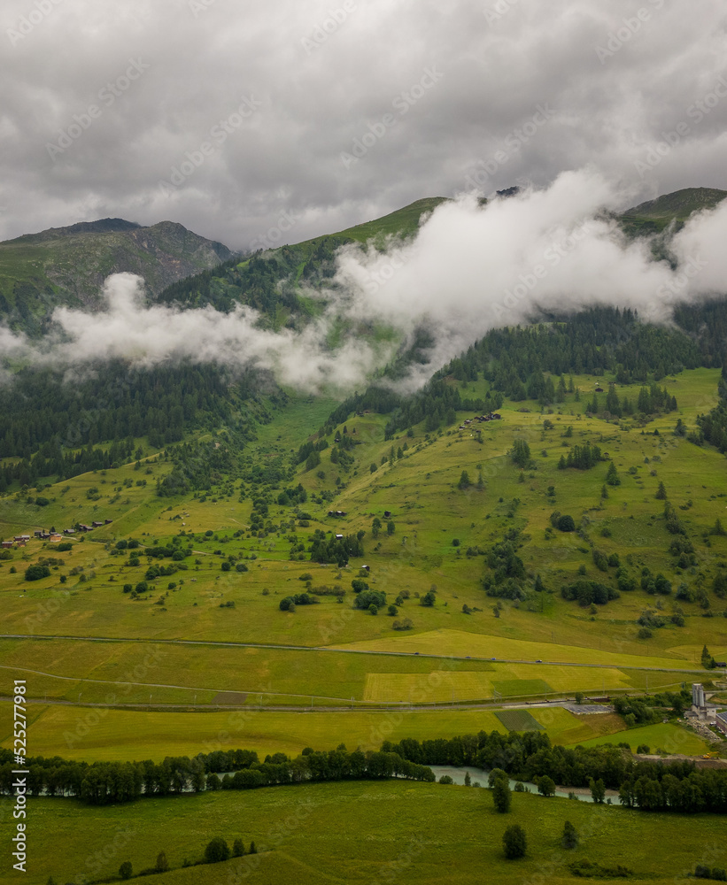 Green Swiss mountain valley with fields and low-hanging clouds. The ...
