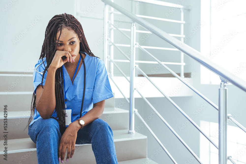 Shot of a young nurse looking stressed out while sitting at a window in ...