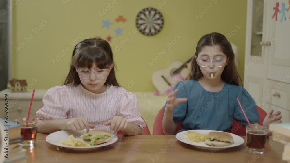 Little girls doing school homework are eating hamburgers. Little kids ...