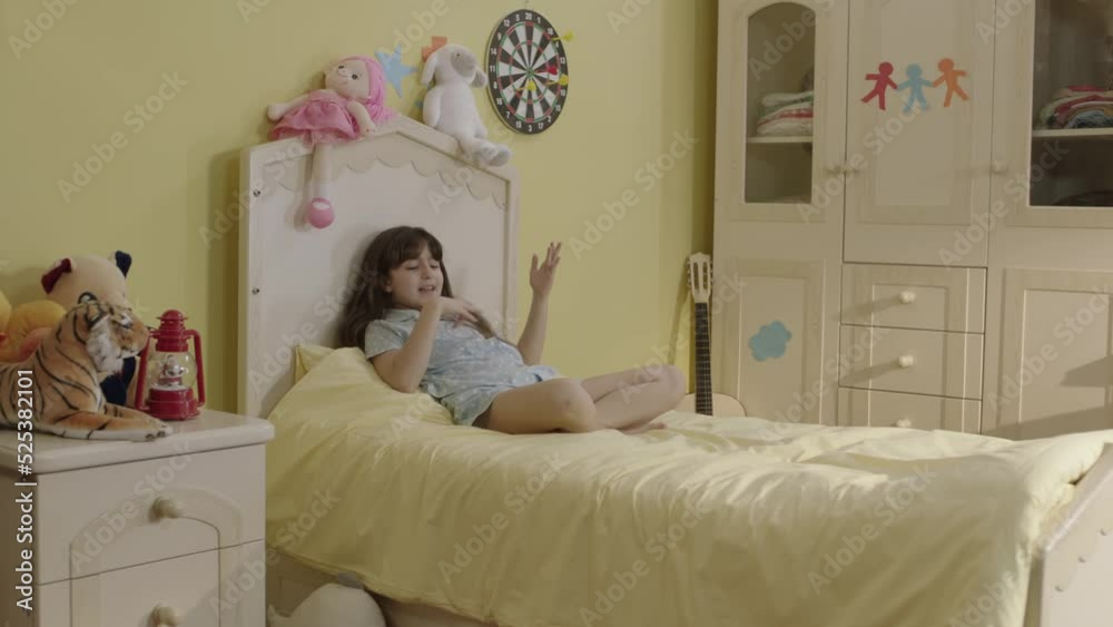 Little girl sings alone in her bed playing an imaginary guitar. Using ...