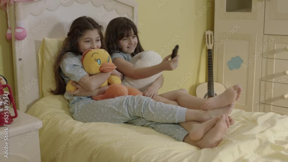 Two little sisters watching an exciting movie wrapped in their plush ...