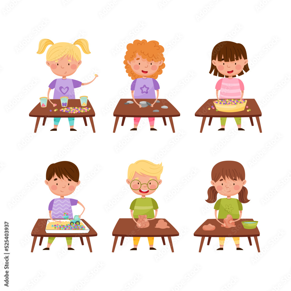 Cute kids standing at table and playing with beads, stones and sand set ...