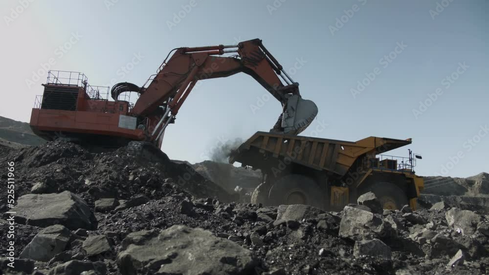 Excavator lifts bucket filled with coal and pours it into mining truck ...