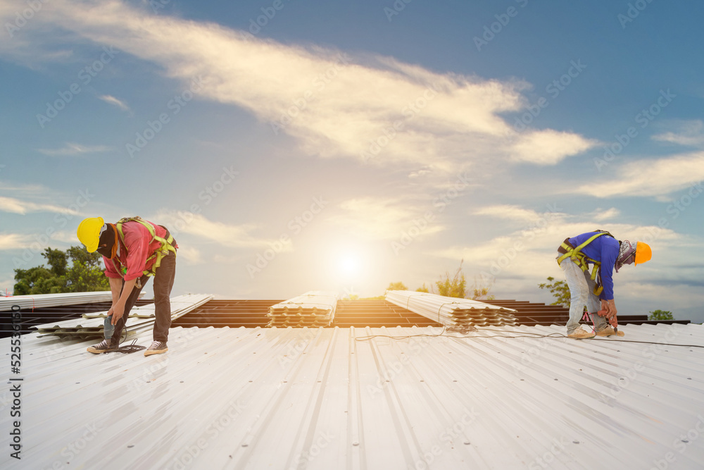 Two construction workers installing a new roof wear safety vests and ...