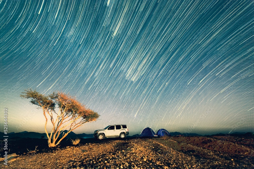 Off-road car and tents on a hill under a starry night with long ...