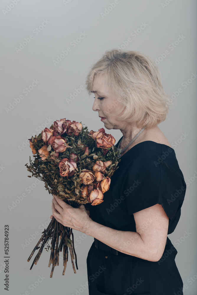 Sad elderly senior woman in white shirt holds withered one dry old dead ...