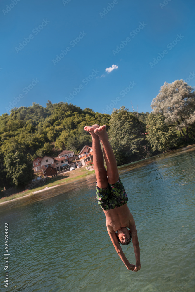 Young teen boy jumping flying and diving in the river. Clear blue sky ...