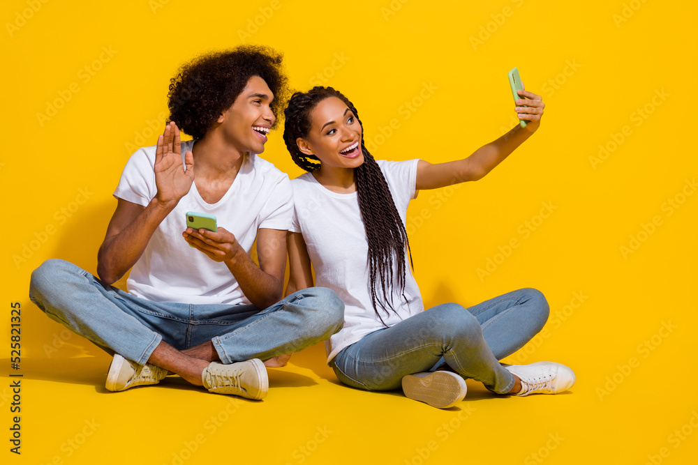 Full size photo of two cheerful people sit floor make selfie arm waving ...