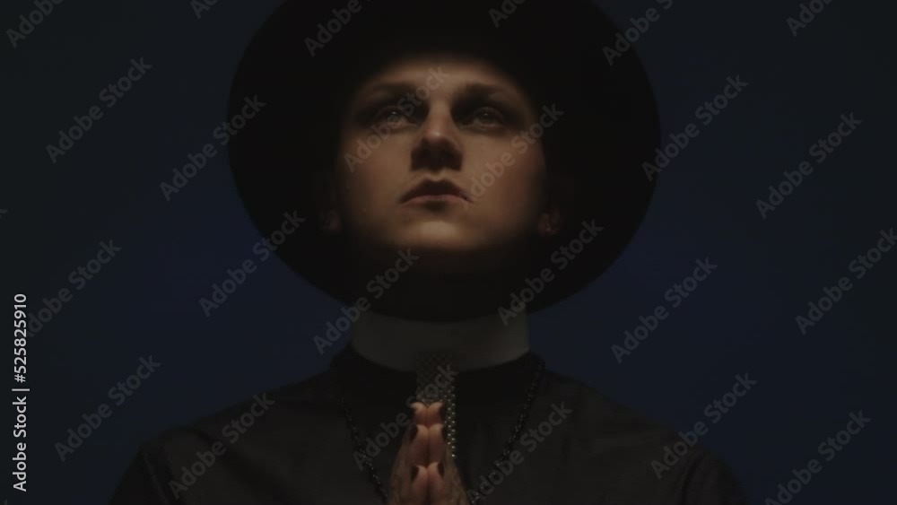 Side view of Catholic priest wearing hat and cassock looking up while ...