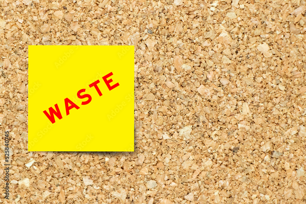Yellow note paper with word waste on cork board background with copy ...