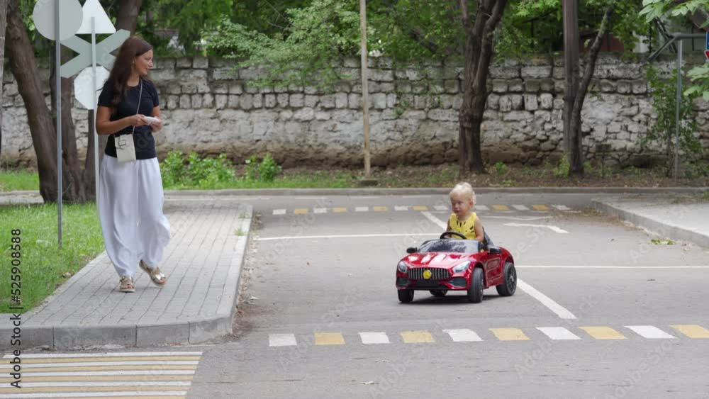 Mother and child have fun learning to ride electric toy car in park ...