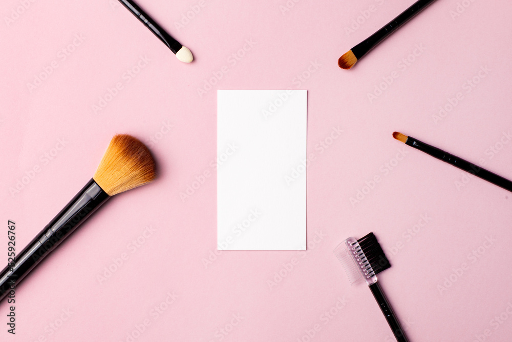 Makeup brush and white business card on pink background. A horizontal ...