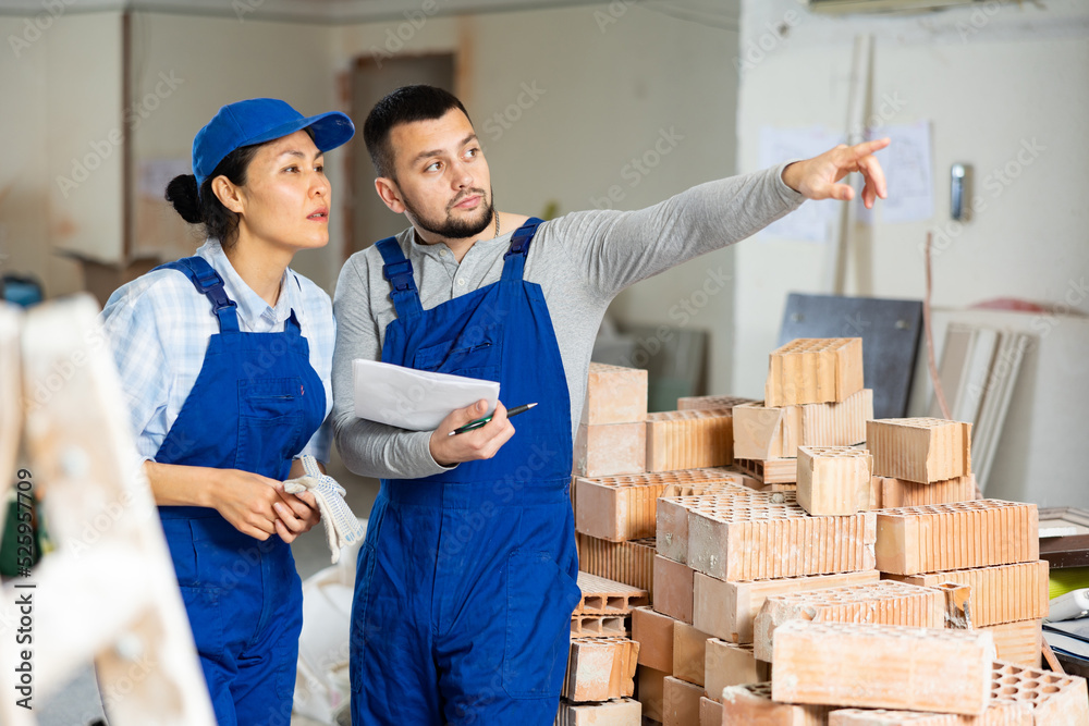 Focused skilled female and male builders in blue overalls determining ...