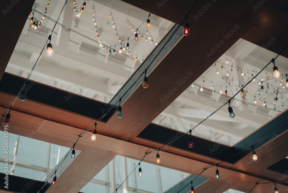 Toned photo colorful light bulb string on ceiling near glass roof and ...