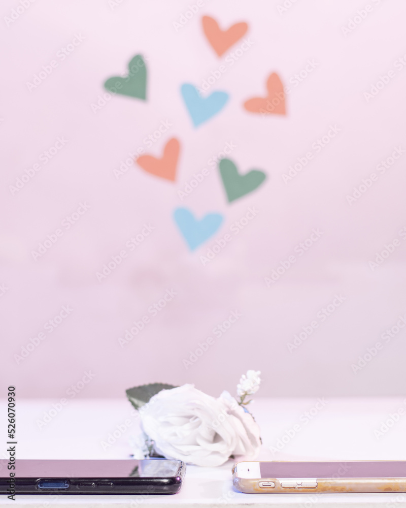 two phones next to each other on a desk, love shapes floating above ...