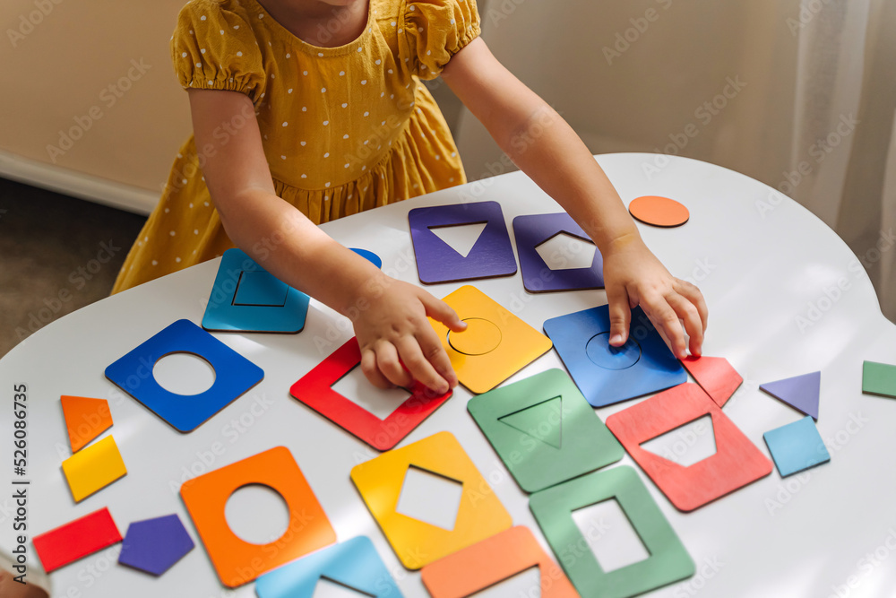 A little girl playing with wooden shape sorter toy on the table in ...