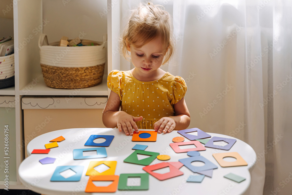 A little girl playing with wooden shape sorter toy on the table in ...