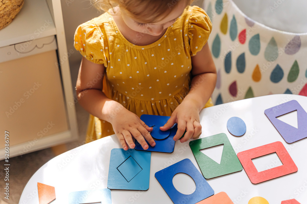 A little girl playing with wooden shape sorter toy on the table in ...