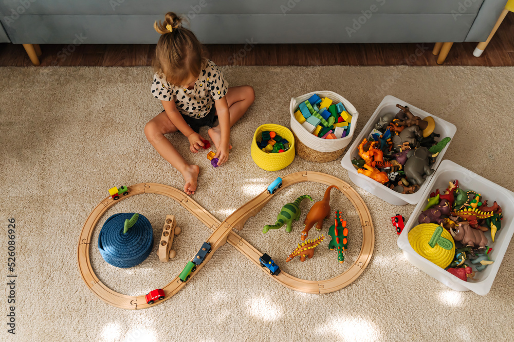 Kid girl builds a toy town and wooden railway. A little girl sitting on ...