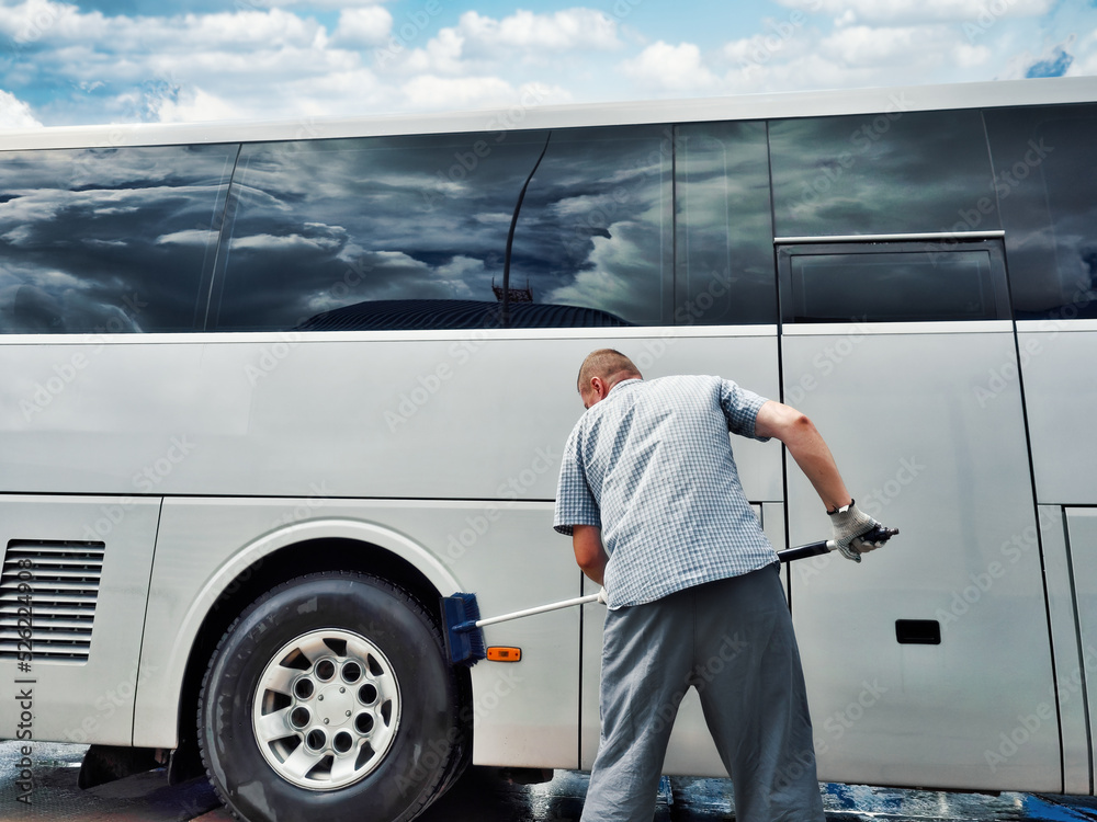 driver washes large bus with brush in open parking lot on summer day ...