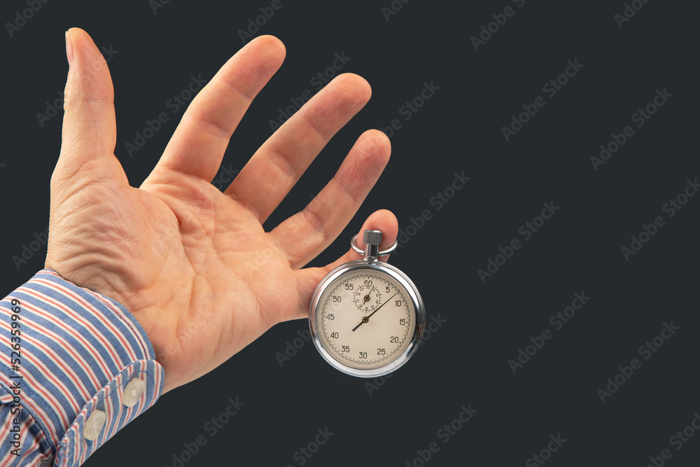 hand with a mechanical analog stopwatch on a dark background. Time part ...
