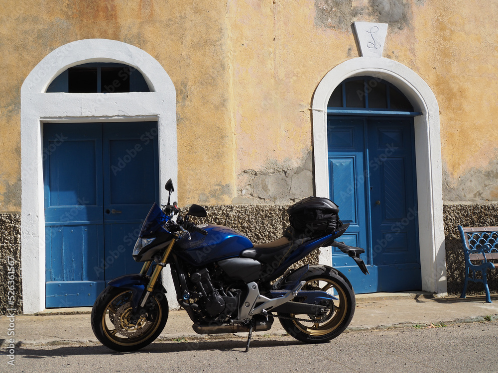 moto roadster sportif bleu arrêté devant une façade aux portes bleues ...