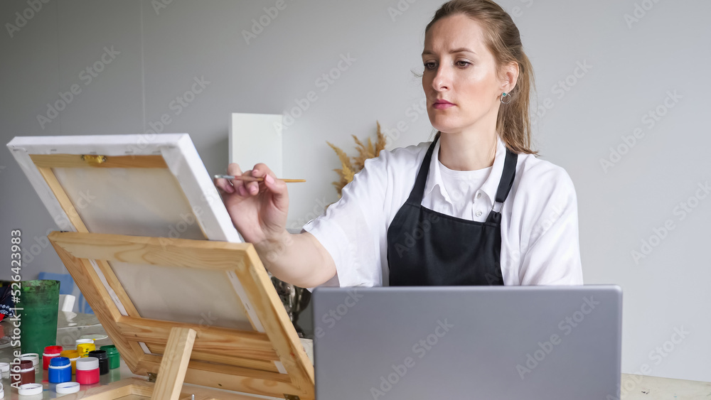 Mature woman artist redraws picture on canvas with paintbrush looking ...