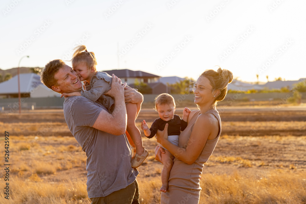 young parents with two young kids in golden light with houses in ...