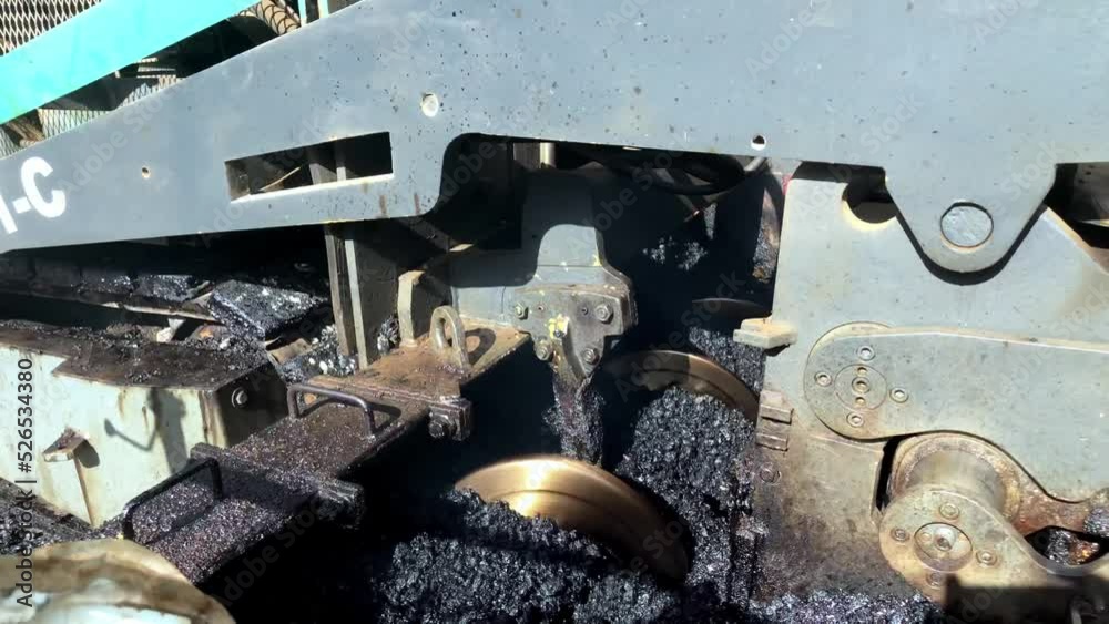 Close-up of auger mixes hot asphalt mix inside of asphalt paving ...