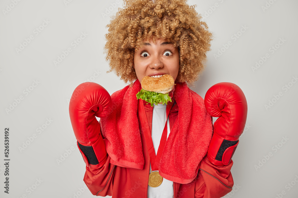 Indoor shot of female boxer eats appetizing burger after fight feels ...