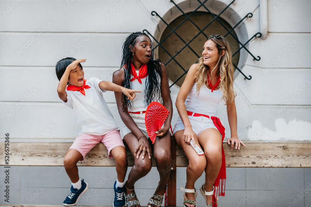 a boy and two girls of different ethnicity, sitting on a wooden barrier ...