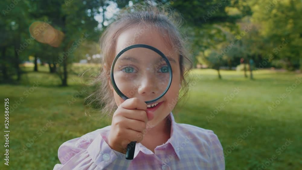 Cheerful little girl looks with magnifying glass camera in the park ...