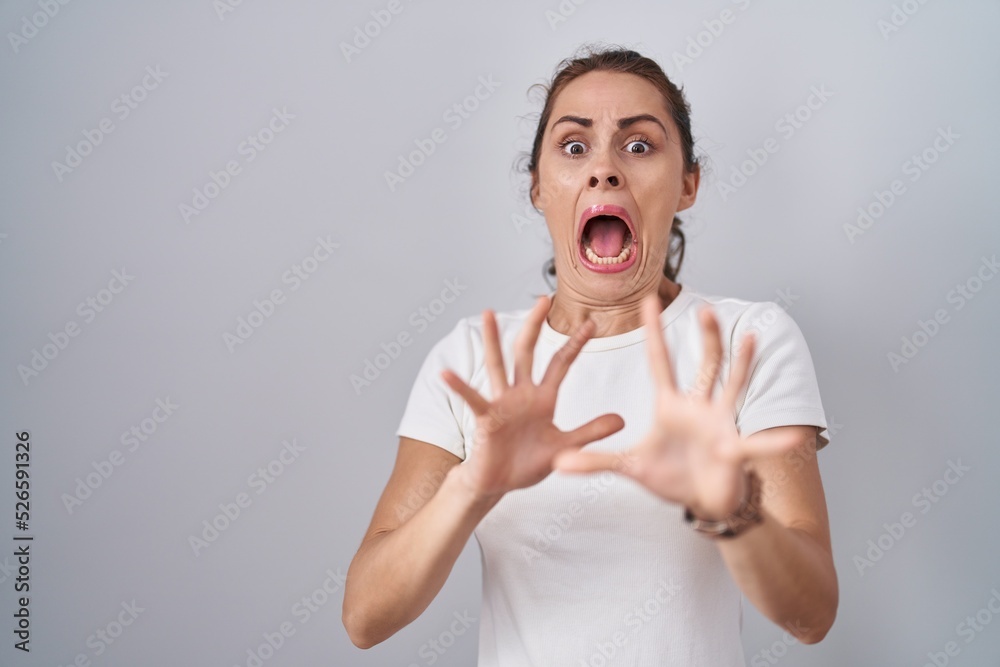 Beautiful brunette woman standing over isolated background afraid and ...