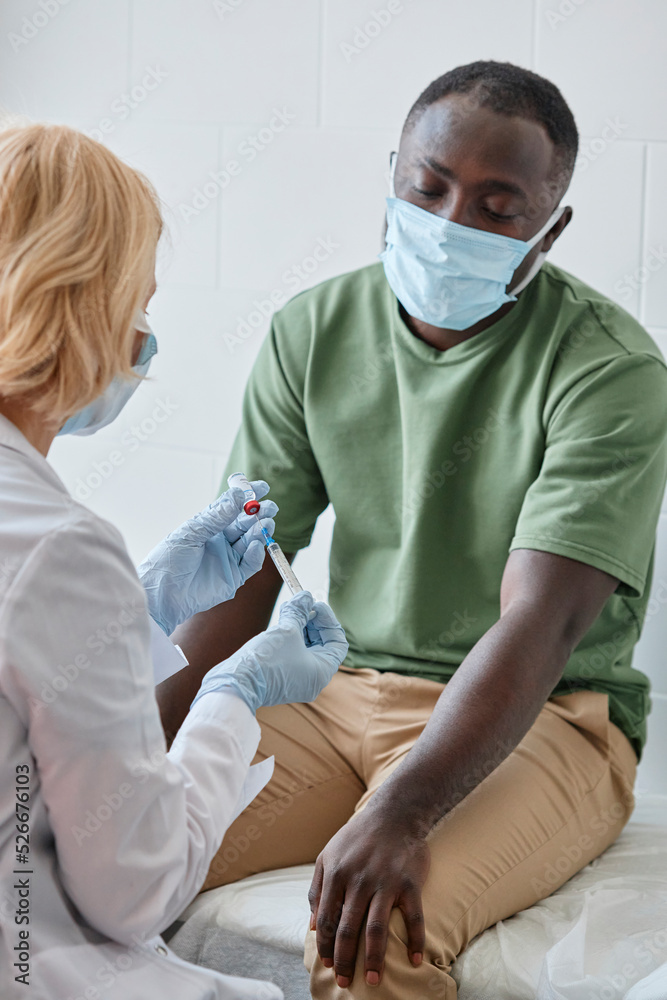 Patient sitting on bed with doctor preparing vaccine syringe in clinic ...
