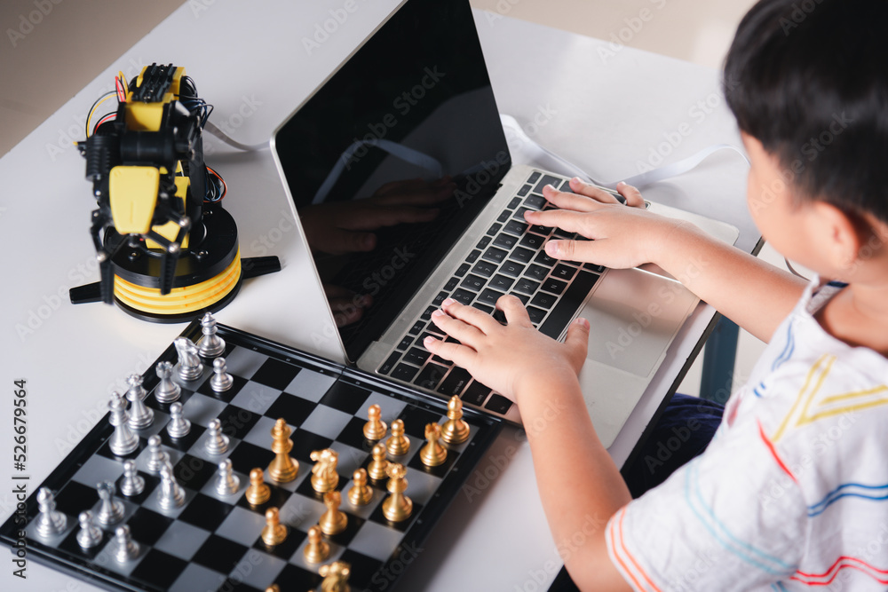 Asian little boy programming code to robot machine arm on laptop for ...