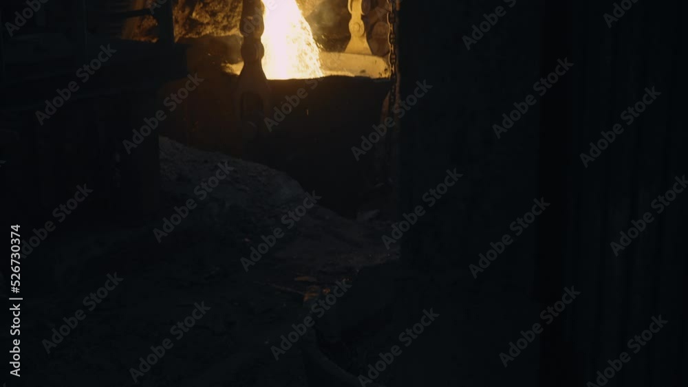 Molten metal flows from the furnace into the ladle. Sparks splatter ...