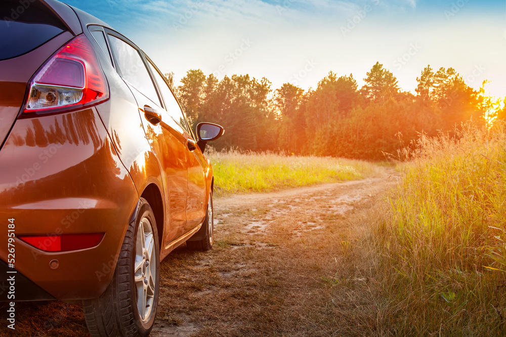 Car in the field at sunset. Close-up of an orange car on a country road ...